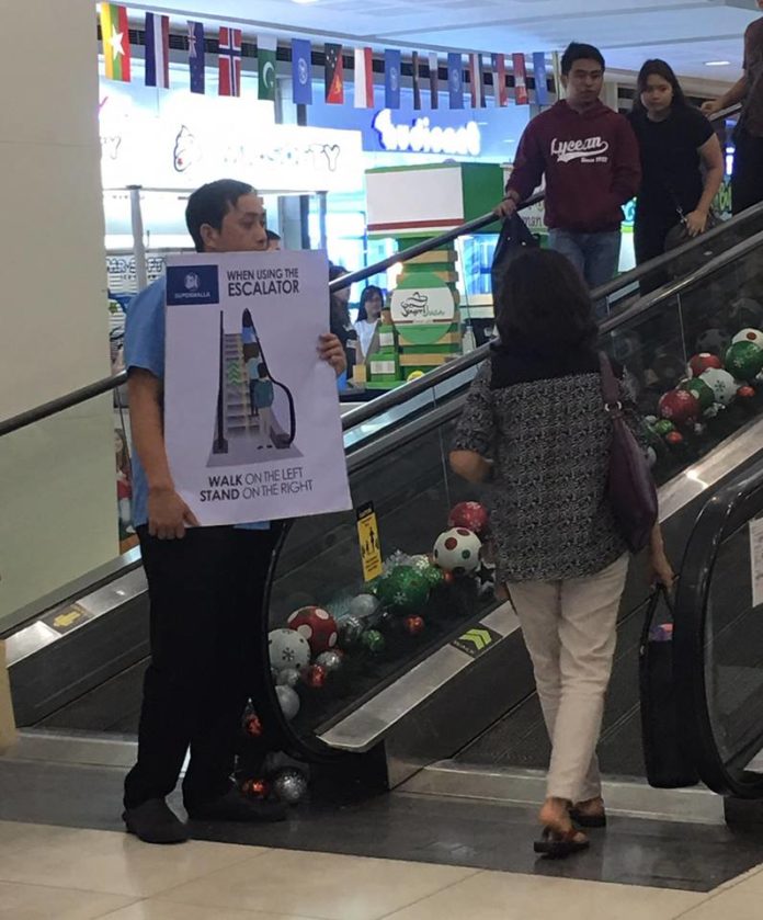 SM Employee Carries Signage At The Foot Of Escalator Area Goes Viral!